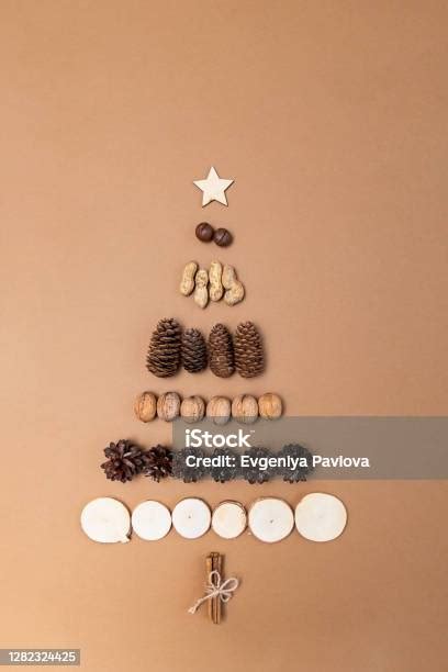 전나무와 소나무 콘 호두 마카다미아 땅콩 계피 스틱 및 베이지 색 배경에 나무 조각으로 만든 에코 스타일의 크리스마스 트리 텍스트를위한 공간이있는 크리스마스 구성 플랫 레이