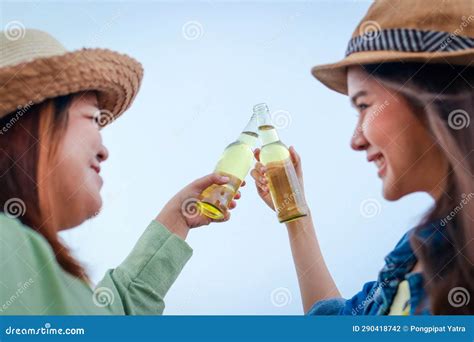 Two Asian Women Partying At Evening Beach Holding Beer Bottles Smiling Happy Having Fun Together
