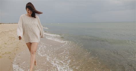 니트 스웨터를 입고 차가운 바다 파도에 모래 사장에서 바람이 부는 머리를 하고 즐거운 시간을 보내는 평온한 아름다운 여성 세련된 젊은 행복한 여성이 해안에서 휴식을 취하고