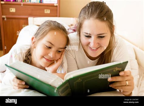 Portrait Of Smiling Mother And Daughter Reading Big Book At Bed Stock