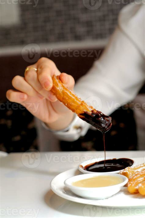 A Hand Dipping Spanish Churros To Warm Dark Chocolate Sauce 23740606