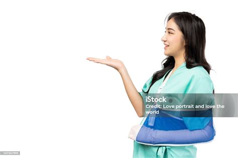 부상당한 젊은 아시아 여자는 손바닥에 상상의 복사 공간을 잡고 광고를 삽입합니다 흰색 배경에 고립 된 부상당한 환자 소녀는 팔이 부러져 부드러운 부목을 착용했습니다 보험