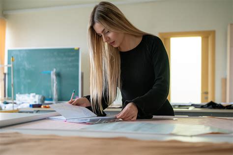 스튜던트 디자이너는 옷감과 도구로 가득 찬 조명이 밝은 작업장에서 메모를 작성하면서 의상 디자인을 만드는 데 집중했습니다 25 29세에 대한 스톡 사진 및 기타 이미지