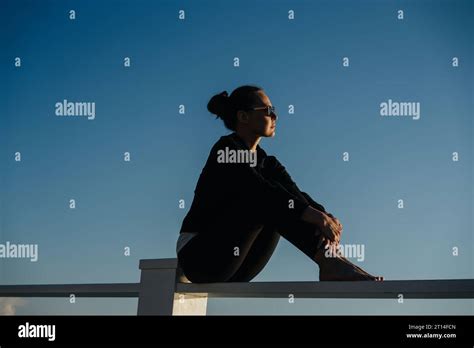 Woman Hugging Her Knees Sits On The Railing Looking At The Sunset