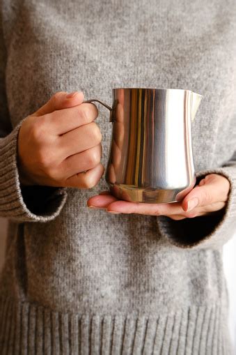 여자는 그녀의 손에 금속 우유 투수를 들고 바리스타 우유 투수 클로즈업 금속 우유 용기 우유 거품기 카페에서 음료 뜨거운 음료 커피를 만들기위한 장비 커피 하우스 전문