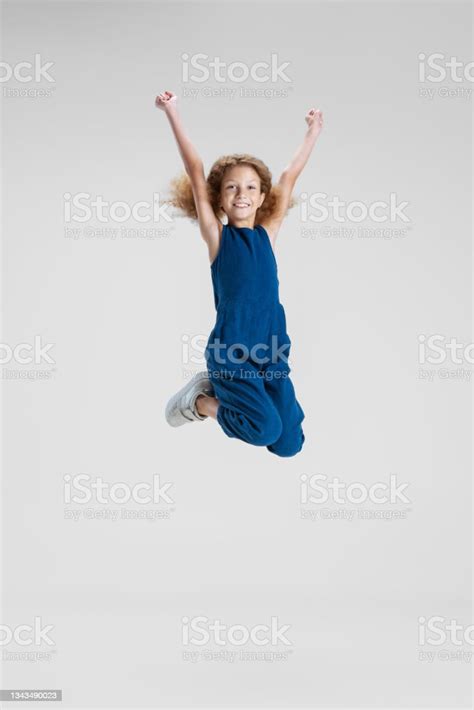 파란색 세련된 점프 수트를 입은 한 작은 백인 귀여운 소녀는 높이 점프하고 흰색 스튜디오 배경을 통해 고립 된 재미를 가지고 있습니다 8 9 살에 대한 스톡 사진 및 기타
