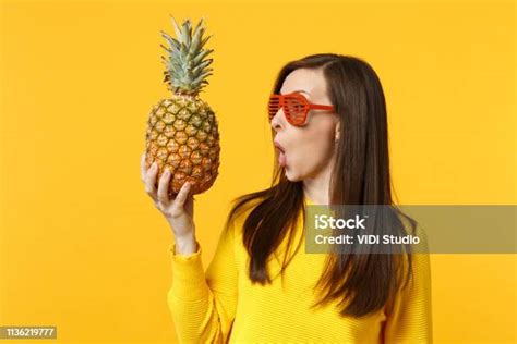 스튜디오에서 노란색 오렌지 배경에 고립 된 손으로 신선한 잘 익은 파인애플 과일을 보고 재미 안경 젊은 여자 충격 사람들은 생생한 라이프 스타일 휴식 휴가 개념입니다 복사