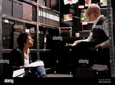 Overworked Police Officers Analyzing Federal Files In Arhive Room Working Late At Night At