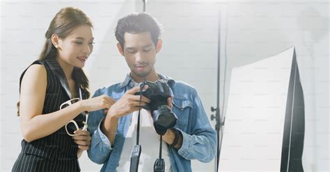 스튜디오에서 전문 사진 촬영 장면 뒤에 아름다운 젊은 아시아 모델이 웃고 메이크업 아티스트와 함께 포즈를 취하고 있습니다 메이크업 사진 작가가 디지털 카메라로 사진을