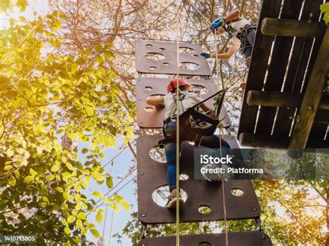 해피 등반 어드벤처 파크에서 활동을 즐기는 십대 소녀는 여름날 안전 장비와 헬멧 사이의 밧줄 다리를 따라 걷습니다 나무 숲에있는 로프 공원 모험 공원이 닫힙니다 모험심