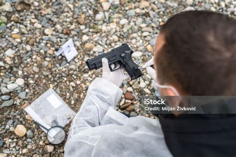범죄 현장의 경찰 형사 법의학 수사관의 윗모습은 수사 복사 공간 중에 살인이나 총격에 사용 된 해변이나 모래 바위에 총기 증거를 보유하고 있습니다 30 34세에 대한 스톡