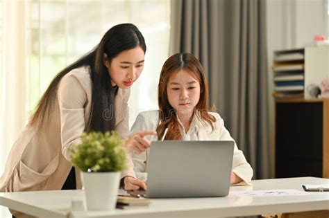Two Female Colleagues Looking At Laptop Screen Collaborating On