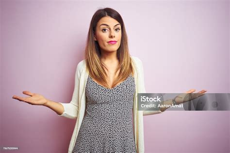 분홍색 고립 된 배경에 서있는 젊은 아름다운 여성은 단서가 없고 두 팔을 벌려 혼란스러워하며 아무 생각도하지 않습니다 갈색 머리에 대한 스톡 사진 및 기타 이미지 Istock