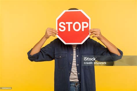 주의 금지 된 방법 스톱 기호 뒤에 얼굴을 숨기고 데님 셔츠에 알 수없는 사람 빨간색 교통 표지판 경고 가리기에 대한 스톡 사진