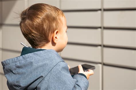 소포 사물함 근처에 휴대 전화를 들고있는 소년 쇼핑 사물함에서 소포를 수집합니다 휴대 전화의 어린이 스칸 Qr 코드 바코드 리더 현대 배송 개념과 휴대 전화 셀프 서비스