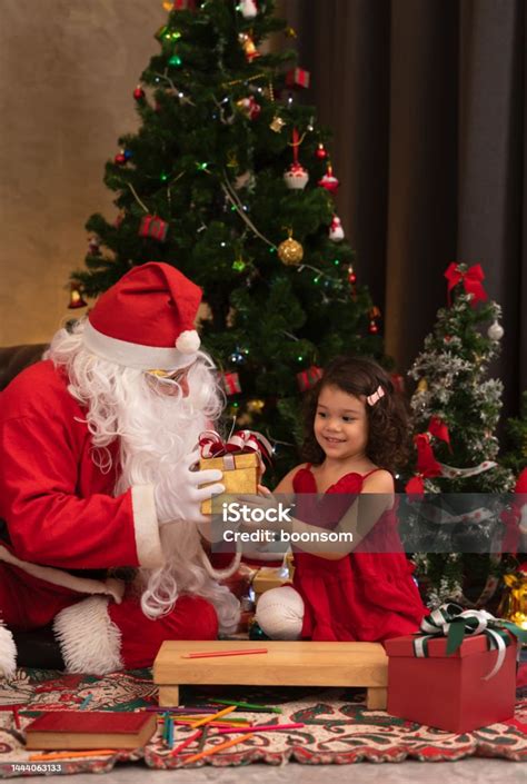 크리스마스 트리 근처에서 귀여운 소녀에게 선물을 주는 산타클로스 집에서 아늑한 따뜻한 겨울 저녁 휴일 크리스마스와 추수 감사절 파티를 축하하십시오 12월에 대한 스톡 사진