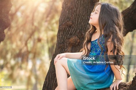 신발 없이 파란 드레스를 입고 공원에서 놀고 있는 아름다운 행복한 소녀는 아이들의 날을 즐기는 가족들과 함께 행복하게 비명을 지르며 나무에 앉아 있다 4 5세에 대한 스톡