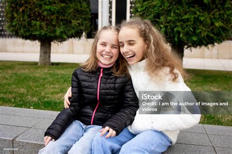 두 자매 소녀가 공원의 벤치에 앉아 서로 껴안고 즐겁게 웃고 있습니다 아이들 사이의 성실하고 따뜻한 관계 10 11세에 대한 스톡 사진 및 기타 이미지 Istock