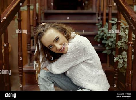 Young Gen Z Woman Sitting On The Stairs In A Spacious Living Room In A