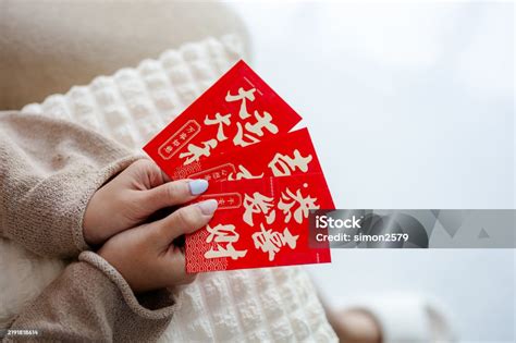 세 개의 빨간 봉투 또는 앙 파오를 들고 있는 여성의 손은 중국의 음력 설날 행사를 상징합니다 한자는 번영과 부를 기원하며 모든 것이 원하는 대로 진행된다는 의미입니다