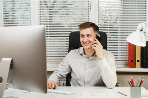 웃는 비즈니스 남자 셔츠는 책상에 앉아 즐거운 대화 현대 모니터 문서 창 배경에 빛 사무실에 있는 컴퓨터에서 작업을 실시 휴대 전화에 대 한 얘기 경영자에 대한 스톡 사진