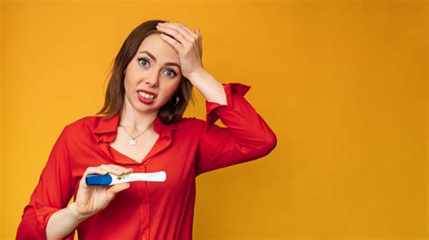 그녀의 손에 긍정적 인 임신 테스트기를 가진 감정적 인 젊은 여성의 스튜디오 샷 그의 얼굴에 어리둥절한 표정 임신 모성의 개념