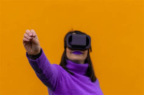 가상 현실 고글을 쓴 웃는 여성의 초상화는 노란색 배경에 손으로 상상의 무언가를 집어 올리는 제스처로 표시됩니다 손에 선택적 초점 25 29세에 대한 스톡 사진 및 기타