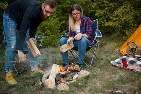 아름 다운 커플 앉아 캠프 파이어 주위에 캠핑 텐트와 배경에 남자 막대기로 화재 제스처 2명에 대한 스톡 사진 및 기타 이미지 Istock
