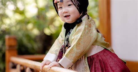 집 밖의 귀여운 나무 녹지 목조 난간 문화 유산 문화 전통 문화적 복장 미소 짓는 사랑스러운 소녀 아기 아기 모자 아기 패션 아기의 첫 번째 생일