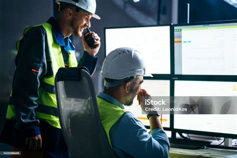 공장에서 안전 조끼와 하드 모자를 착용 한 주요 엔지니어 및 근로자 운영자는 Scada 시스템 및 Industry 40을 사용합니다 두 명의 연산자가 Ui가있는 화면을