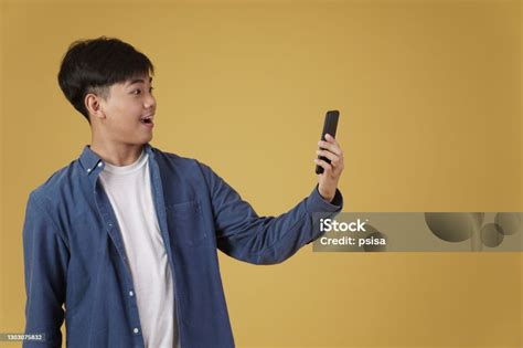 노란 배경에 고립 된 스마트 폰을 캐주얼하게 보고 자연스럽게 옷을 입은 행복한 놀란 젊은 아시아 남자의 초상화 20 24세에 대한 스톡 사진 및 기타 이미지 Istock