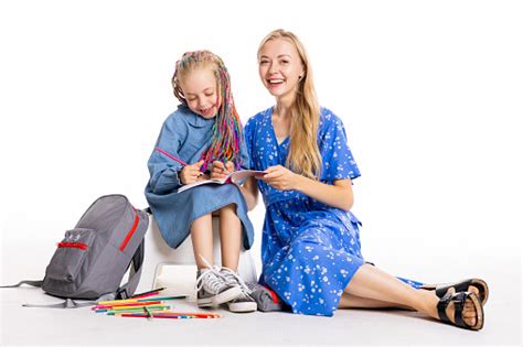 스튜디오의 하얀 바닥에 앉아 있는 행복한 여학생은 스튜디오에서 어머니와 함께 학교 개념으로 격리된 숙제를 쓰고 있다 행복한 가족 2명에 대한 스톡 사진 및 기타 이미지