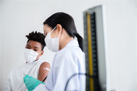 아프리카 남자는 상처를 커버하고 예방 접종 후 주사기를 들고 여성 의사 또는 간호사를보고 석고와 함께 쇼를 앉아 코로나바이러스 19의 확산을 방지하기 위한 개념 2명에 대한