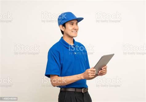 파란색 유니폼을 입은 아시아 남자는 고립된 흰색 배경에 디지털 태블릿 컴퓨터를 들고 서 있다 휴대 전화를 가진 남성 서비스 노동자 택배 배송 서비스 고객에 대한 스톡 사진