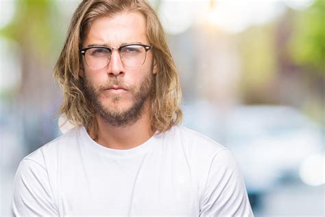 격리 된 배경 회의론 및 교차 팔과 얼굴에 긴장 Disapproving 식 안경을 쓰고 긴 머리를 가진 젊은 잘생긴 남자 부정적인 사람입니다 감정에 대한 스톡 사진 및 기타