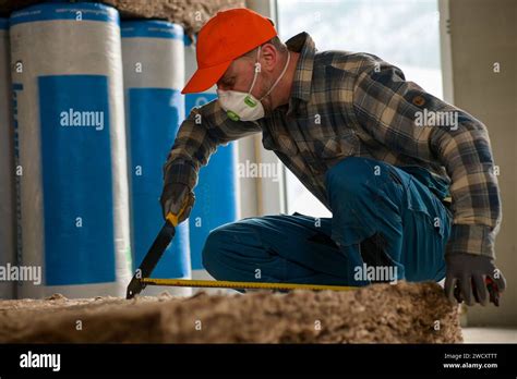 A Worker In Overalls And Gloves Measures The Length Of The Glass Wool