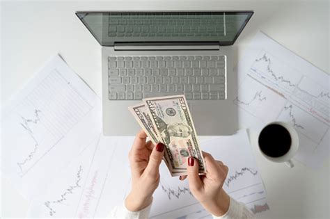 지폐 50 달러의 팩을 손에 들고 이익 소득을 계산하는 여성 프리랜서 사무실 테이블에 종이에 인쇄 된 그래픽과 차트와 노트북 외환 교환 플랫 레이 거래자에 대한 스톡 사진