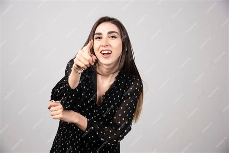 Free Photo A Young Woman Pointing To The Camera On A Gray Wall