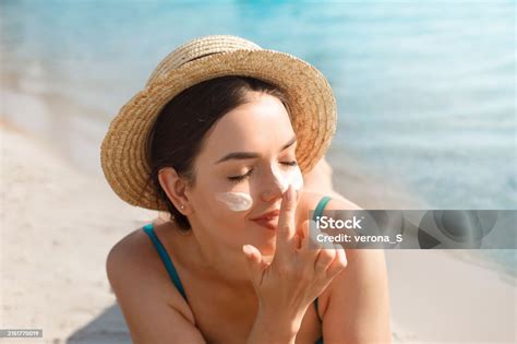 얼굴에 선크림을 바른 아름 다운 젊은 여자 해변에서 자외선 차단제 병을 들고 있는 소녀 모자에 모이스처라이징 로션을 바르는 여성