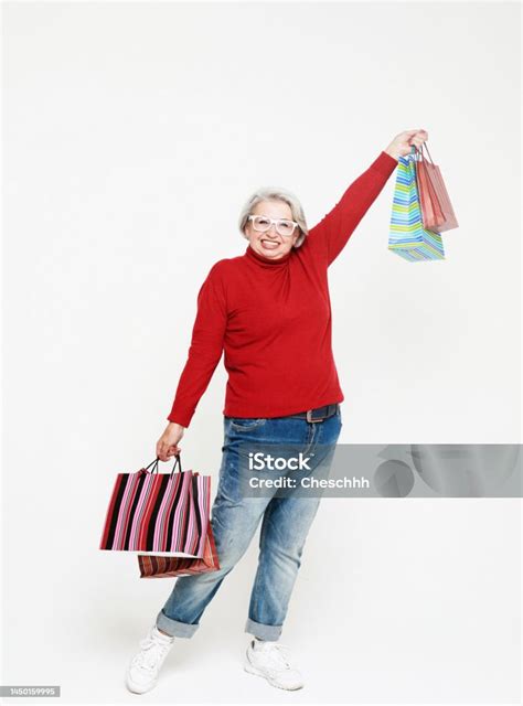 긍정적 인 쾌활한 회색 흰 머리 노인 여성의 전체 길이 사진은 여가 시간 쇼핑 홀드 가방을 청바지와 빨간 스웨터를 착용 65 69세에 대한 스톡 사진 및 기타 이미지