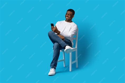 Premium Photo Happy Young Black Man Sitting On Chair Using Cell Phone
