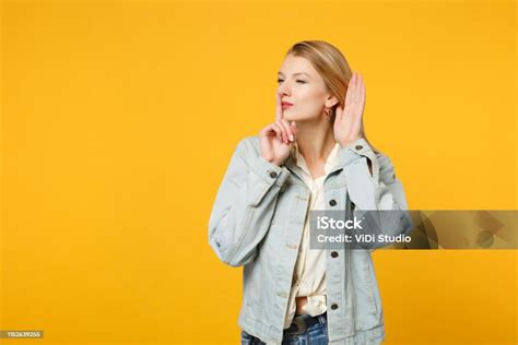 데님 캐주얼 옷에 호기심 젊은 여자는 입술 쉿 제스처에 손가락으로 조용 하 고 노란색 오렌지 벽 배경에 고립 듣기 위해 시도 말한다 사람들 라이프 스타일 개념입니다 복사