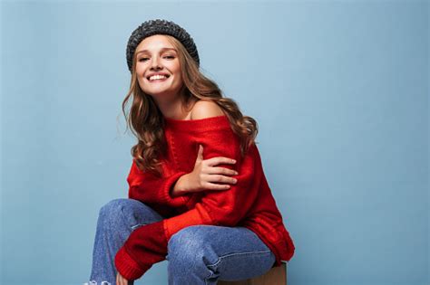 젊은 예쁜 미소 여자 와 물결 모양의 머리 모자와 빨간 스웨터 행복 하 게 찾고 카메라 위에 앉아 파란색 배경 16 17 살에 대한 스톡 사진 및 기타 이미지 Istock