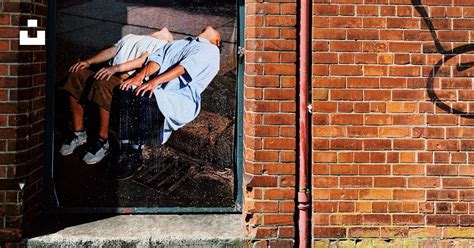 흰색 드레스 셔츠와 검은 바지를 입은 남자가 갈색 벽돌 벽에 앉아 있다 사진 Unsplash의 무료 도시 이미지