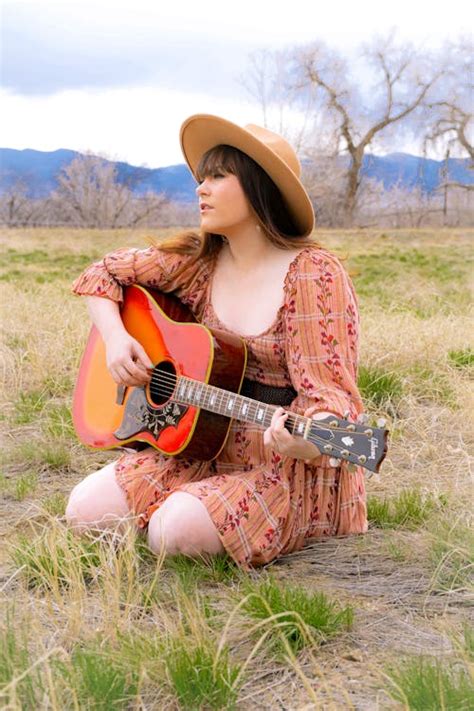 야외에서 어쿠스틱 기타를 연주하는 젊은 여성 · 무료 스톡 사진