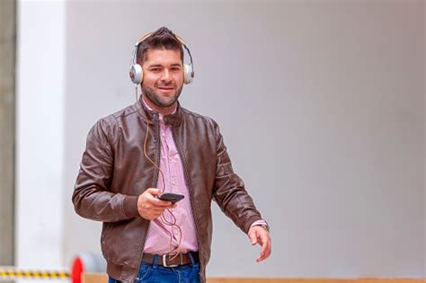 쾌활한 젊은 라틴 아메리카 사무실 노동자는 휴대 전화와 고급 헤드셋을 사용하여 음악을 듣고 그가 출근으로 아침 햇빛에 사무실