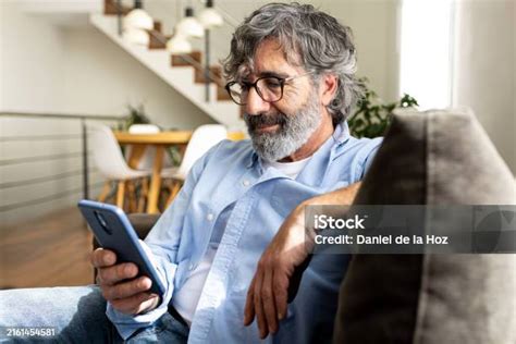 집에서 휴식을 취하고 소파에 앉아 휴대폰으로 문자 메시지를 보내는 성숙한 남자 전화 사용에 대한 스톡 사진 및 기타 이미지 전화 사용 휴대전화 스마트폰 Istock