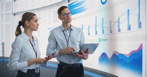 Male And Female Data Analysts Discussing New Locations For Business In Front Of Big Digital