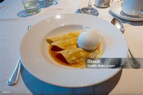 캐러멜 소스를 뿌린 섬세한 크레이프 접시에 바닐라 아이스크림 한 스쿱을 얹고 커피 한 잔과 탄산수 한 잔과 함께 흰색 식탁보에 담겨 제공됩니다 0명에 대한 스톡 사진 및