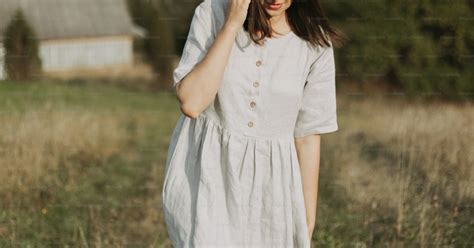 린넨 드레스와 모자를 쓴 세련된 소녀가 마을의 햇볕이 잘 드는 들판의 풀밭에서 맨발로 걷고 있다 시골에서 휴식을 취하는 보헤미안 여성 소박한 소박한 삶 대기 이미지